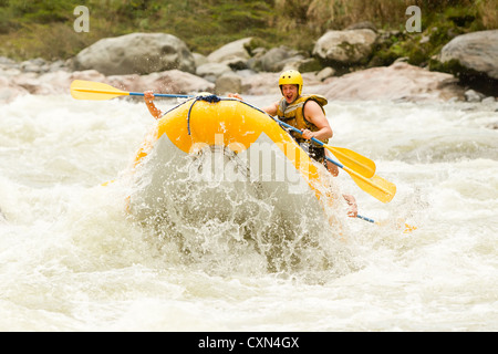 A blue inflatable raft with paddler gripping rope and oar above muddy ...