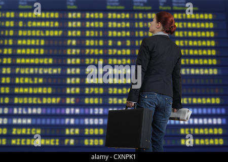 Passenger standing in front of flight information display board showing ...