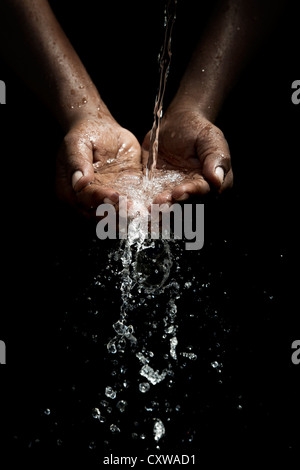 Indian mans cupped hands catching poured water against black background ...