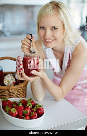 Portrait of woman eating strawberry while leaning on kitchen counter at ...