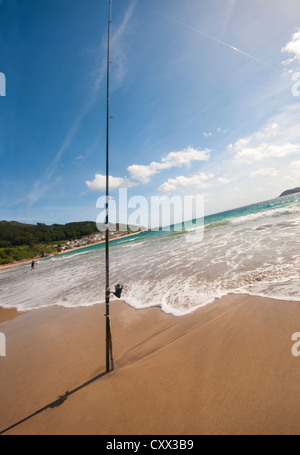 Fixed fishing rod set up on a beach near the surf on the incoming tide ...