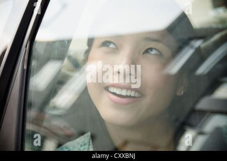 Woman riding in a car, looking at her smartphone and holding a reusable ...
