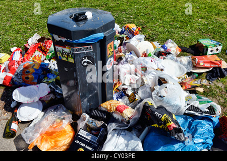 Overfull rubbish bin / garbage can with trash around and beer cans ...