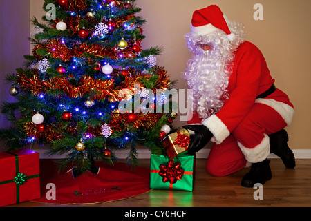 Santa Claus or Father Christmas putting presents under the tree whilst ...