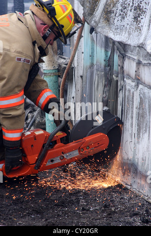 A firefighter using a saw to cut into a metal wall to gain access to a ...