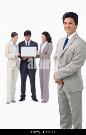 Smiling salesman using laptop with colleagues behind him Stock Photo ...