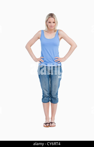Relaxed blonde woman placing her hands in her pockets against a white ...
