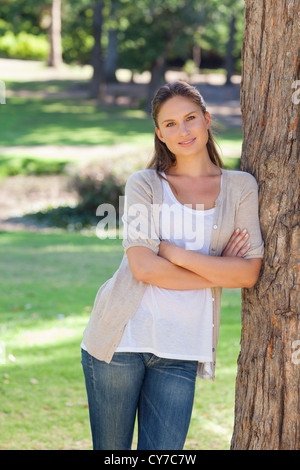 Beautiful woman arms folded leaning against a tree smiling Stock Photo ...