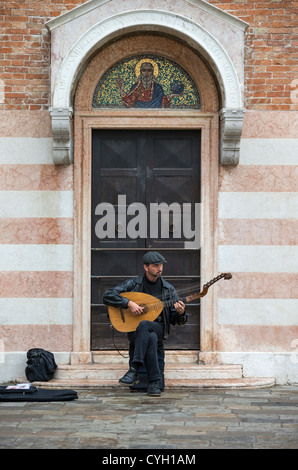 A street musician playing a long-necked lute with a second pegbox ...