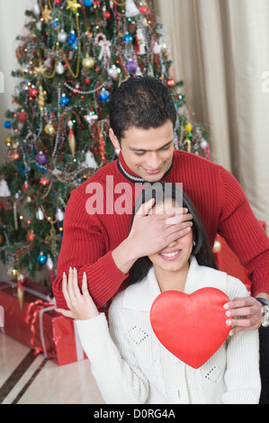Husband covering his wife eyes to give her a surprise gift on christmas ...
