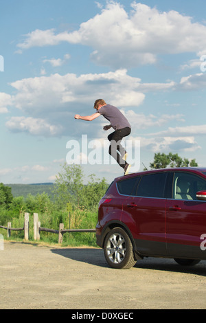 Young man jumping off car roof, girl sitting on roof Stock Photo - Alamy