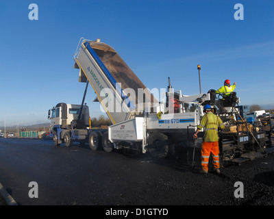 A road paver & tipper truck laying tarmac on the first phase of the ...
