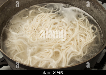 noodles cooking in a pot of boiling water with burning foam almost ...