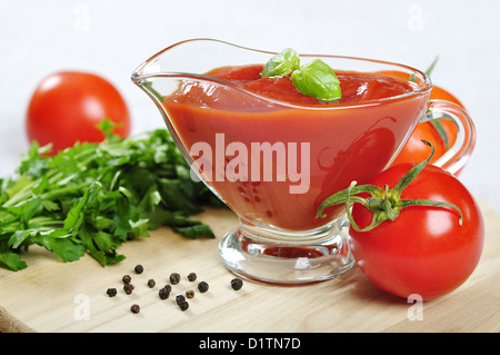 Tomato sauce in a glass gravy boat with fresh tomatoes on a wooden tray ...