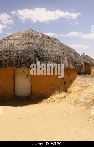 Traditional mud hut with grass roof alongside more modern hut with ...