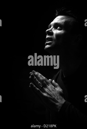 A man kneeling down in prayer against the background of a row of pews ...
