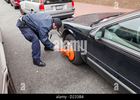 Parking enforcement officer installing a wheel lock on a car ...