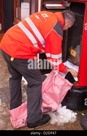 A Royal Mail postman UK emptying mail from a mailbox, with his red ...
