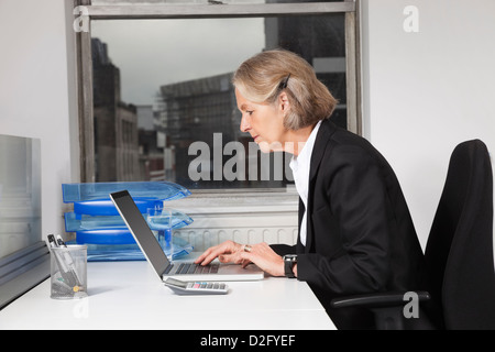 Senior businesswoman using laptop and calculator at desk in office ...