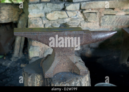 Metal anvil with rust attached to a stump, and a stone wall in the ...