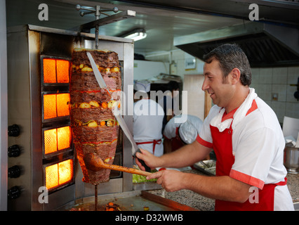 Worker slicing doner kebab from a rotating vertical spit in a kebab ...