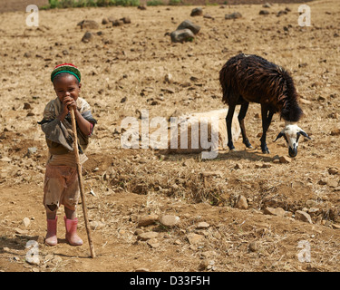A young child stands with a stick playfully on a barren dry shield with ...