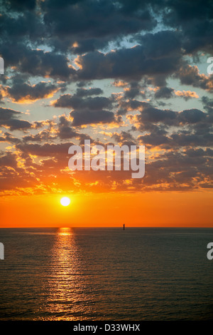 Orange and gold colored sun at sunset over the silhouette of a mountain ...