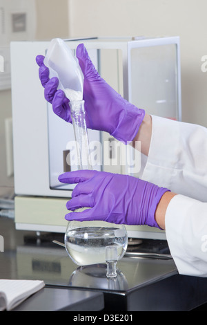 Laboratory scientist adding a solid reagent to a container on a scale ...