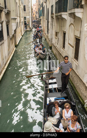 A tourist taking a gondola ride along as the gondolier steers the ...