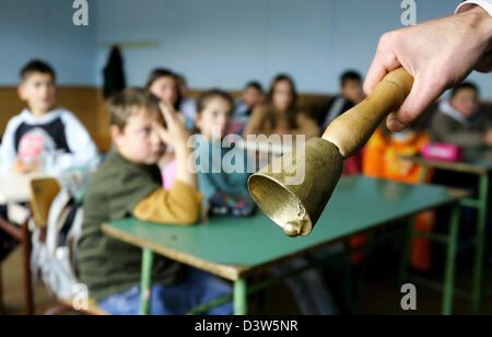 The picture shows a teacher's hand ringing the school bell in a ...