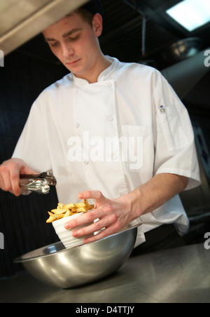A chef working in a restaurant, at the pass preparing plates of food ...