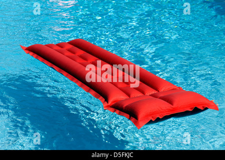 An inflatable red air mattress swimming in a shiny blue swimming pool ...