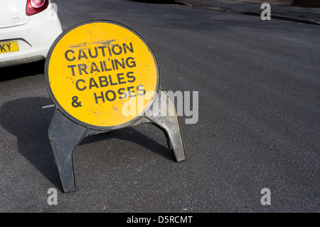 A sign warns of trailing cables and hoses before an area of road works ...