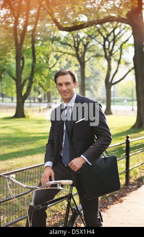 smiling businessman sitting on bicycle in office and looking at camera ...