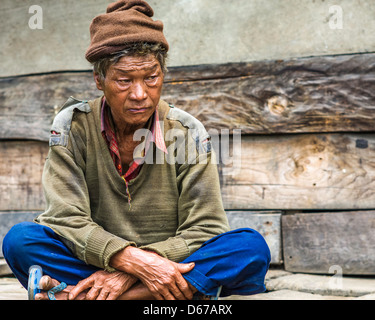 Portrait of man from the Monpa tribe sitting outside his wooden house ...