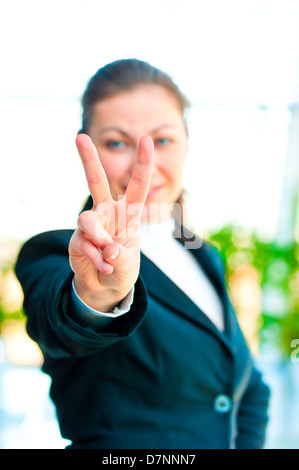 Woman showing victory gesture by her hands isolated on gray background ...