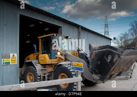 A front end loading shovel exiting an industrial building doorway ...
