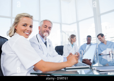 Portrait of two doctors sitting at meeting table by window and taking ...