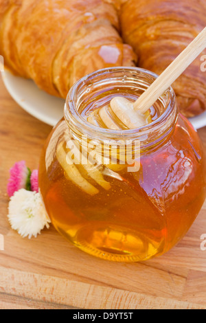 Close up of croissant, honey jar and orange juice on wooden cutting ...