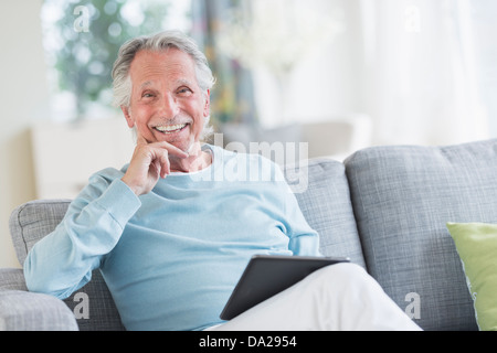 Senior man sitting on sofa with headphones and using laptop Stock Photo ...
