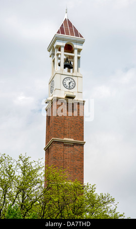 A classic clock tower in a green park setting with a tall building in ...