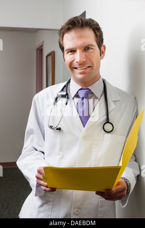 Doctor holding file folder in front of white wall Stock Photo - Alamy