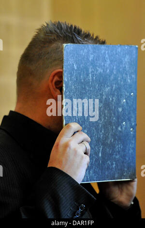 The accused Olaf H. hides his face behind a file in the court room of ...