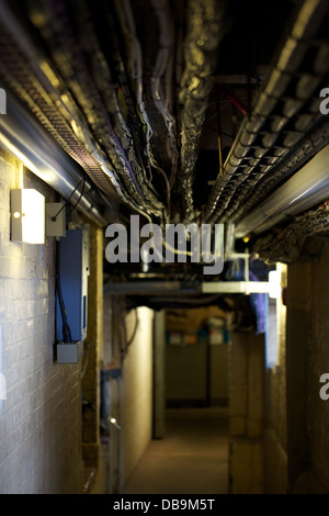An underground basement passage way, dimly lit with pipes and services ...