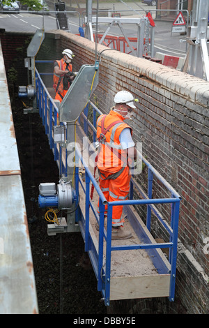 Workmen renovate the brick parapet to a road bridge over a railway ...