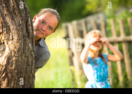 Two sisters playing hide-and-seek, one covering eyes with hands, the ...