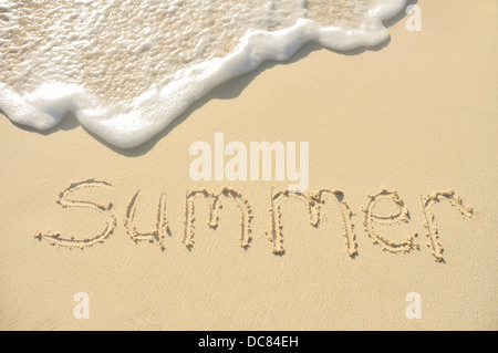 The word "summer" written on the sand by the sea at sunset while a wave ...