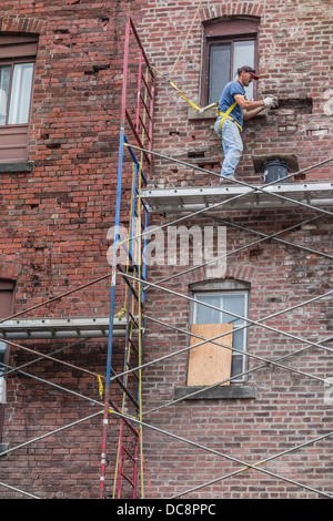 A brick mason works on a scaffolding three stories high to repair a ...