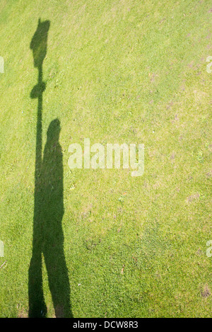 Shadow of a man on a lawn leaning against a lamp post with his hand out ...