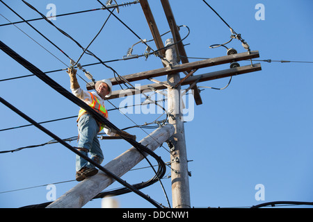 Cable lineman climbing a pole brace to cable bundles on power pole ...